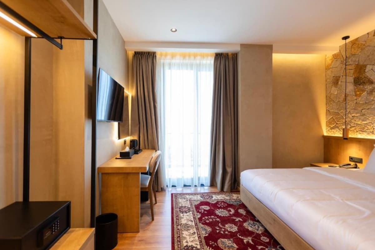 Quarto de hotel com cama, escrivaninha, televisão e parede de pedra.