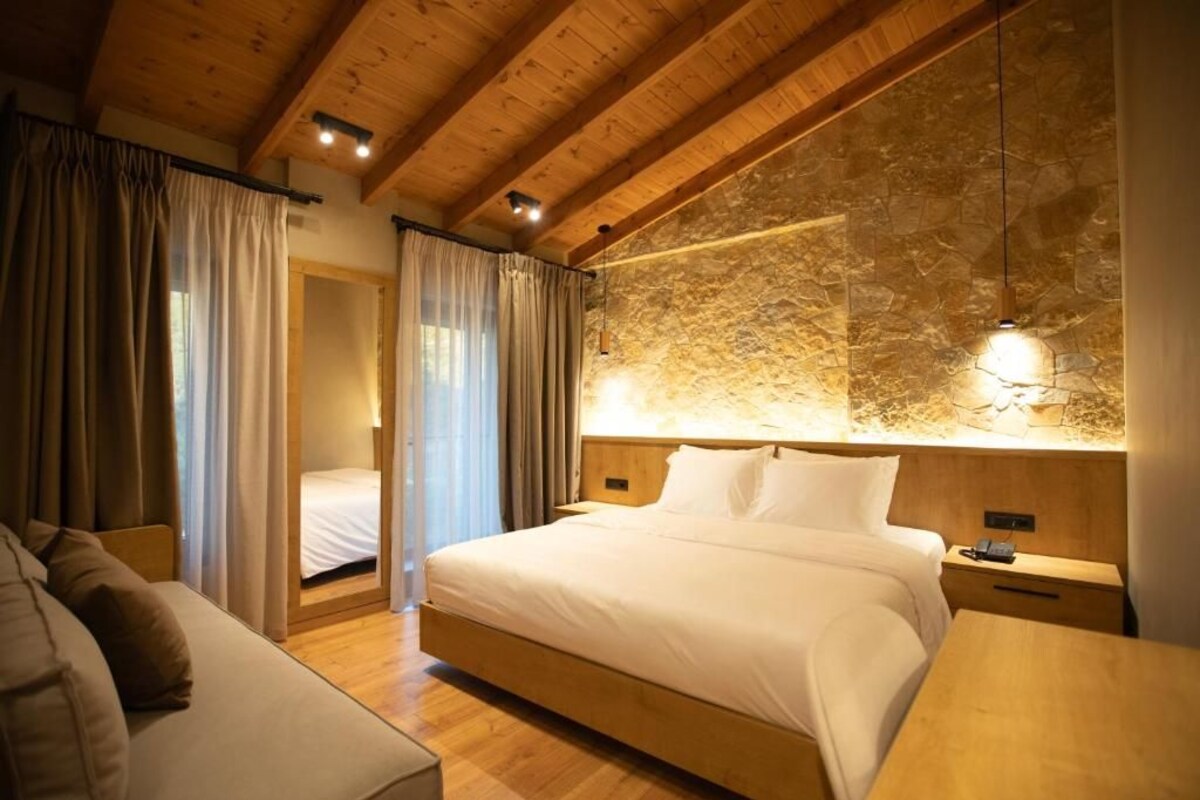 Quarto com cama grande, cabeceira de madeira, mesa de cabeceira com abajur e janela coberta por cortinas.