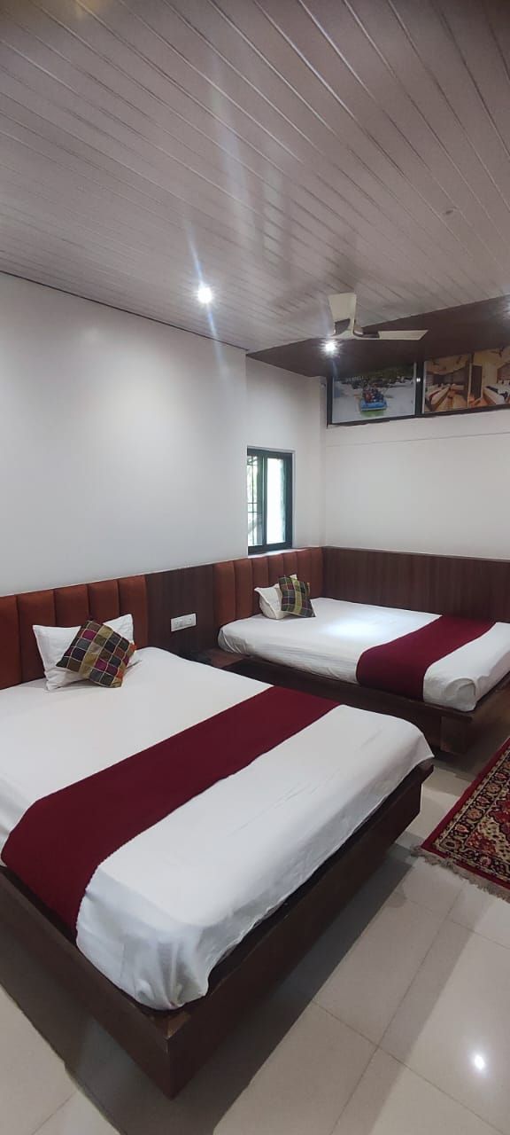 Quarto de hotel com duas camas, ventoinha no teto, janela e tapete vermelho.