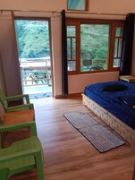 Quarto com cama, cadeira verde, mesa de madeira e vista para uma varanda com mobiliário exterior.