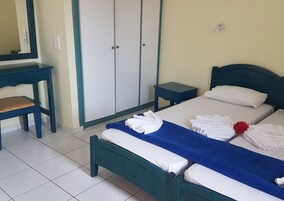Quarto de hotel com cama, escrivaninha, cadeira, guarda-roupa e mesa de cabeceira.