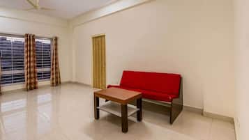 Quarto com sofá vermelho, mesa de madeira, ventilador de teto e janela com cortinas.