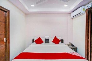 Quarto de hotel com cama, mesa de cabeceira, ar condicionado e porta de madeira.