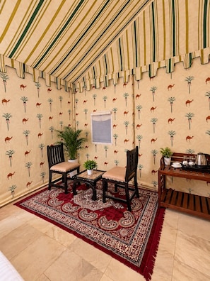 Quarto com papel de parede listrado, duas cadeiras, uma mesa pequena, uma planta em vaso e um tabuleiro com bule e xícaras.