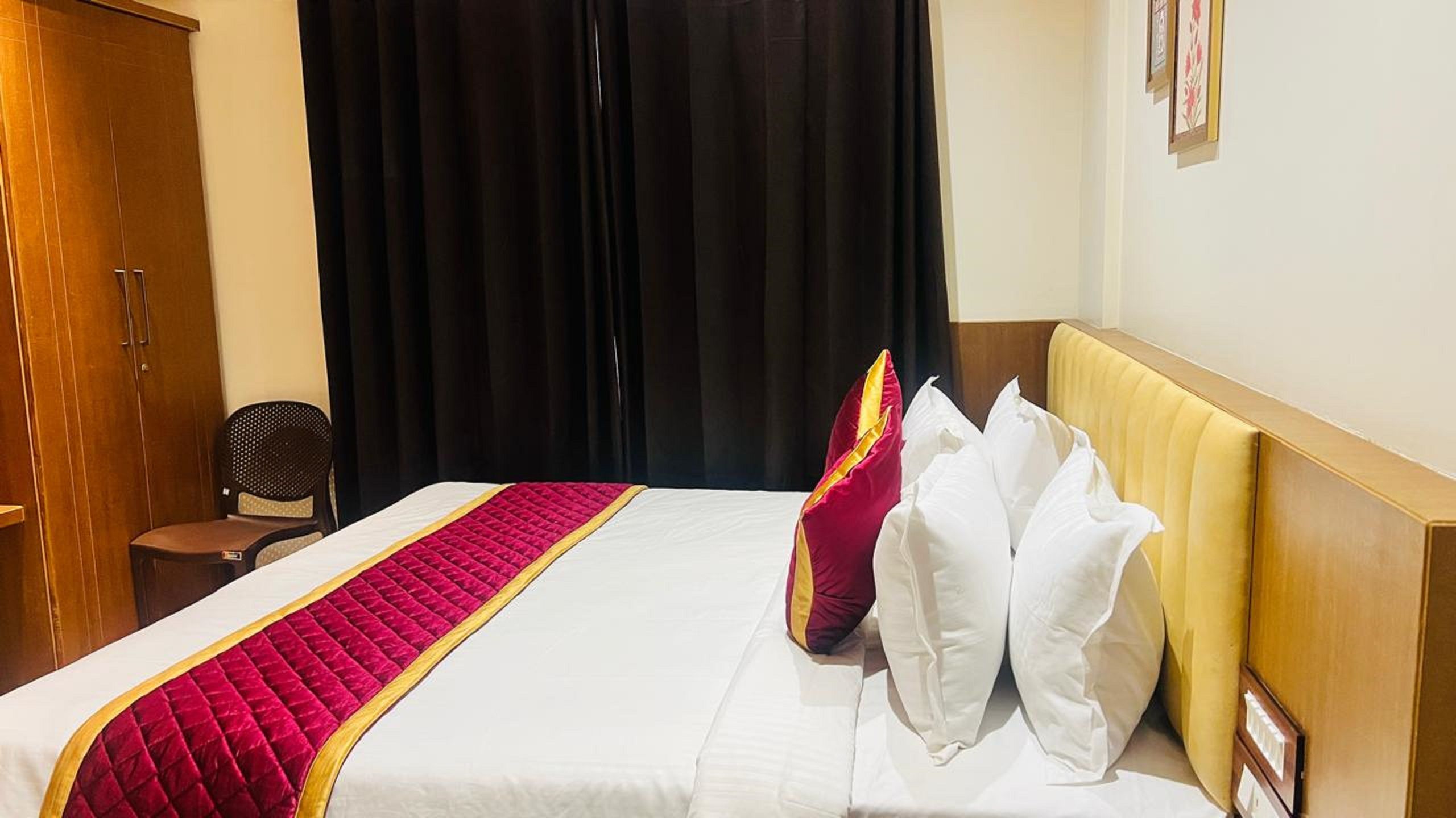 Quarto de hotel com cama, guarda-roupa de madeira, uma cadeira e cortina preta.