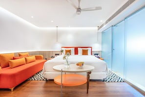 Quarto de hotel moderno com cama, sofá, mesa redonda e ventoinha no teto.