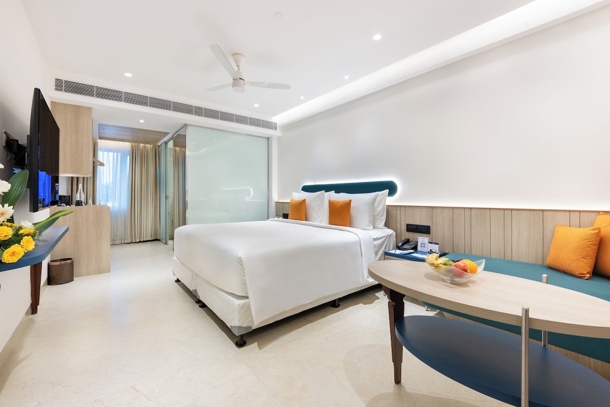 Quarto de hotel moderno com cama, escrivaninha, área de estar e ventilador de teto.