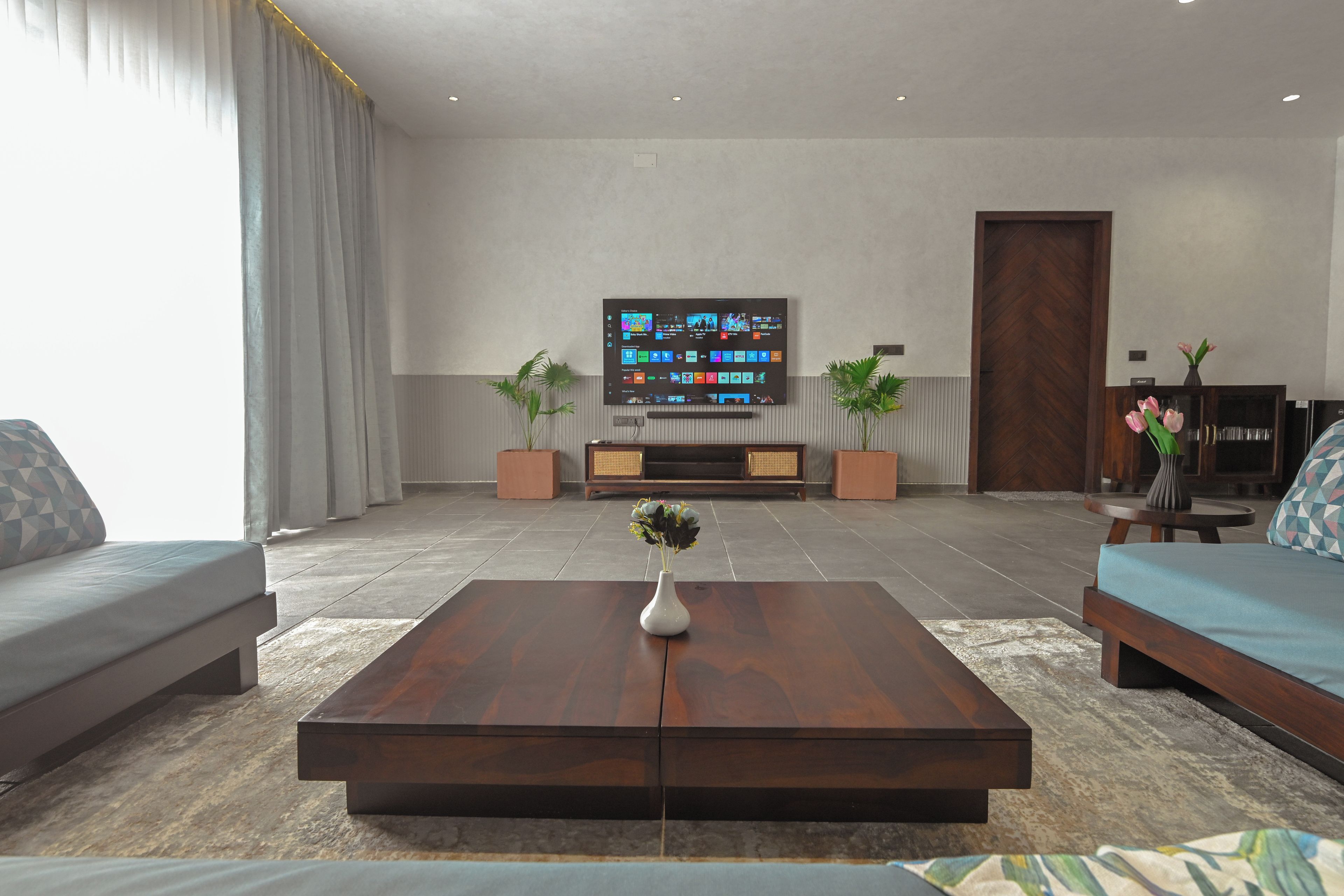 Uma sala de estar moderna com televisão de tela plana, dois sofás, uma mesa de centro e plantas em vasos.