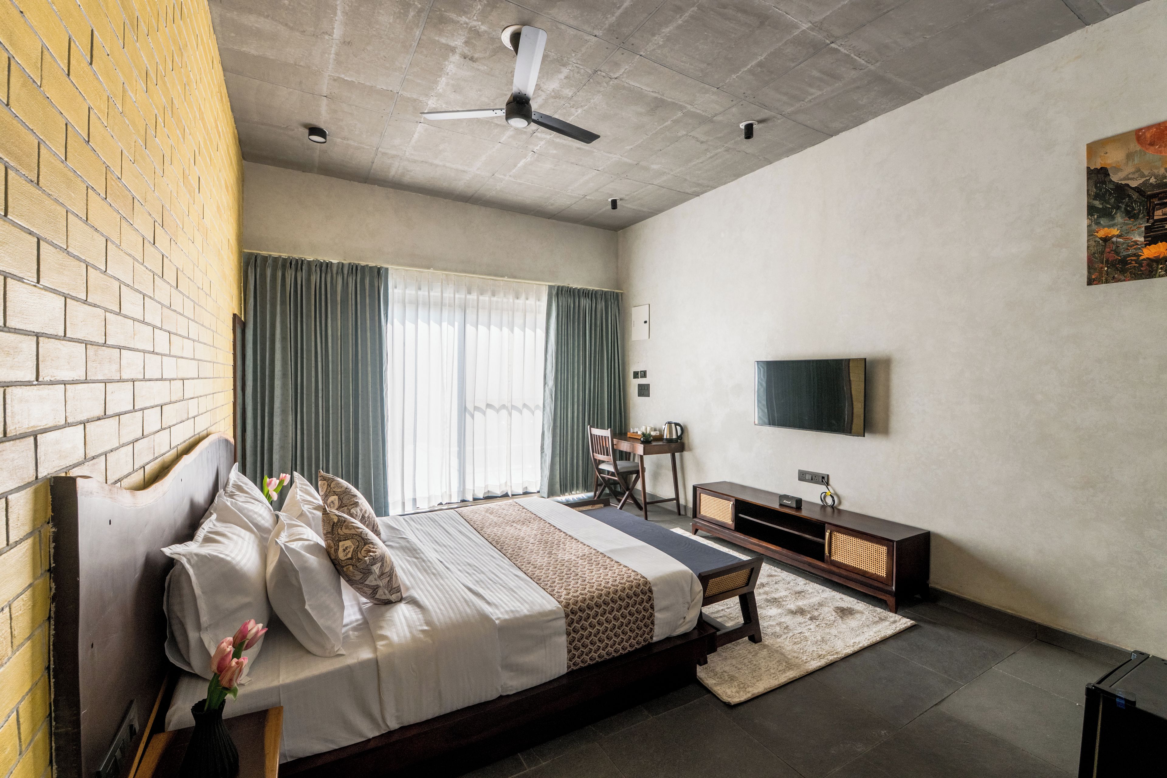 Quarto moderno com cama, escrivaninha, cadeira, televisão e parede de tijolos.