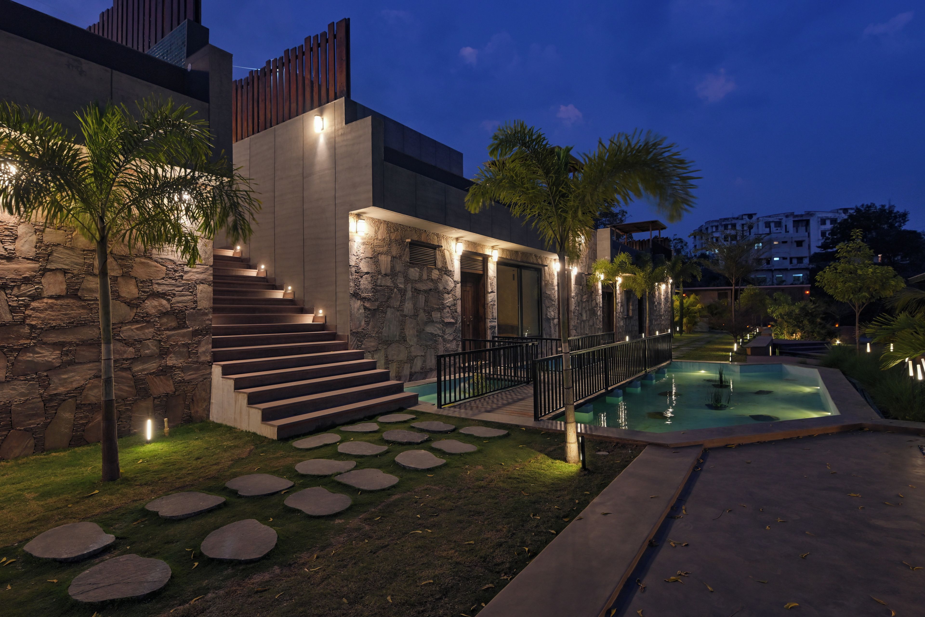 Um edifício moderno com fachada de pedra, piscina e escadaria que leva à entrada.