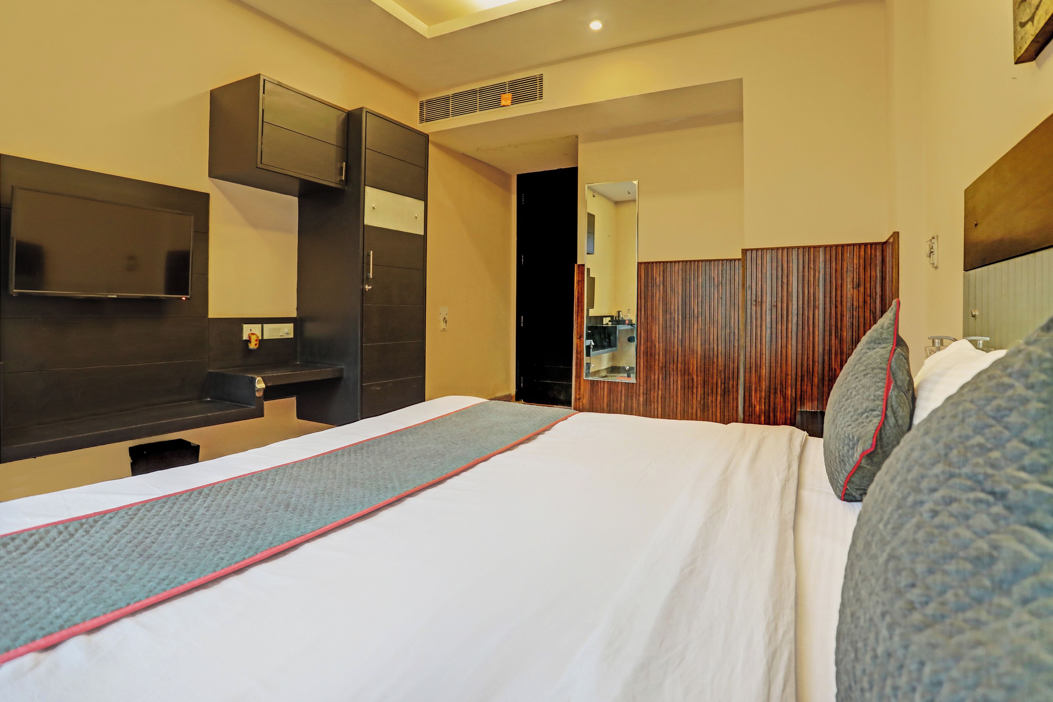 Quarto de hotel com cama, televisão, guarda-roupa e espelho.