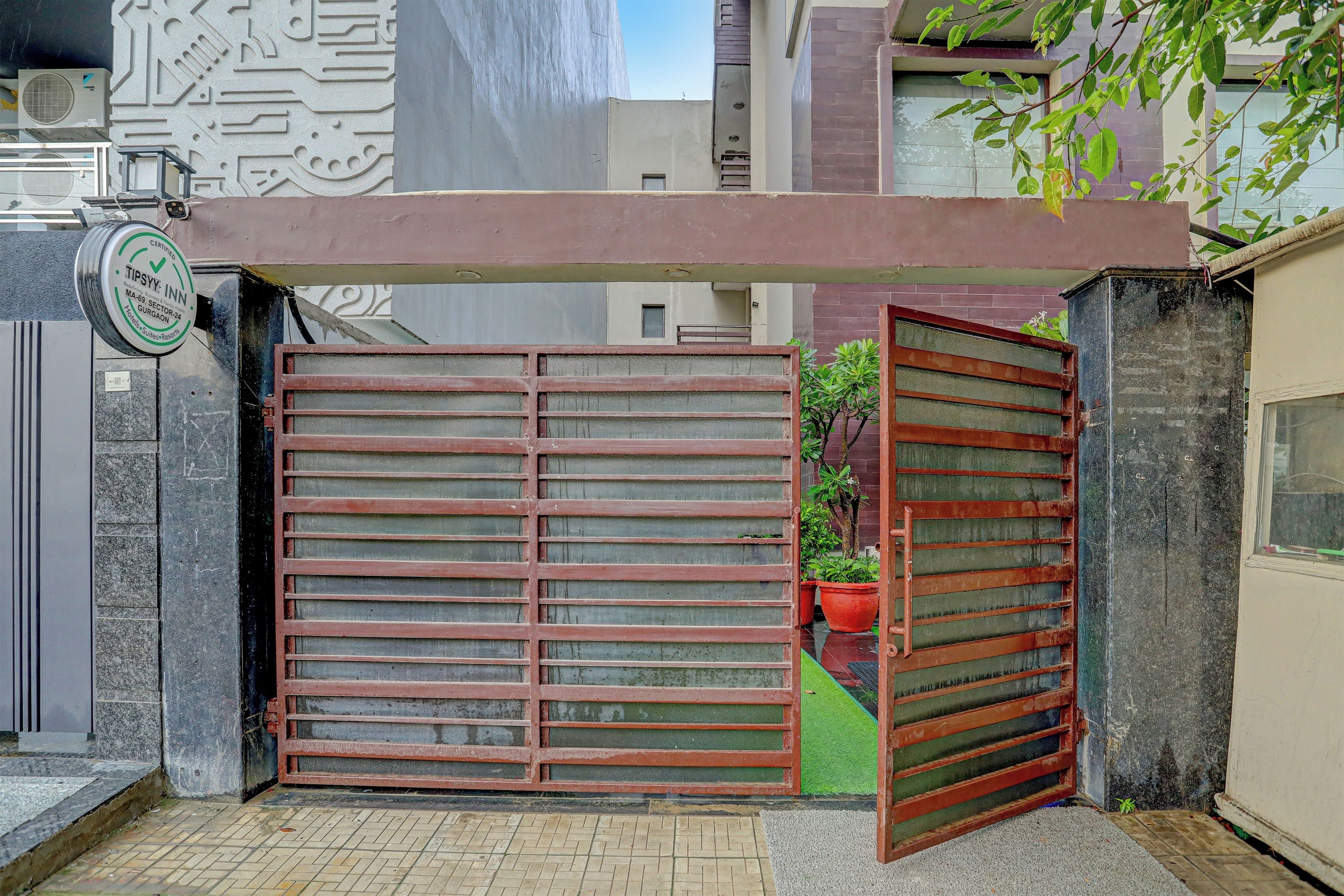 Uma entrada fechada por portão de metal, com uma placa indicando um hotel e uma pequena janela com vista para os edifícios ao redor.