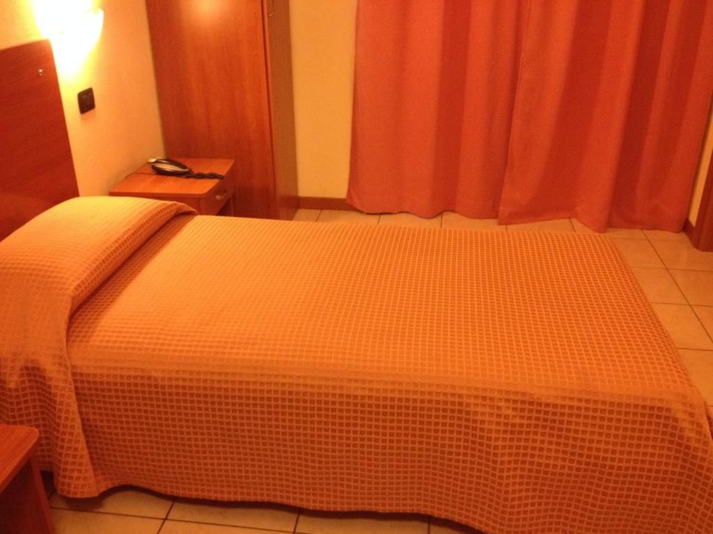 Quarto de hotel com cama, mesa de cabeceira e luminária na parede.