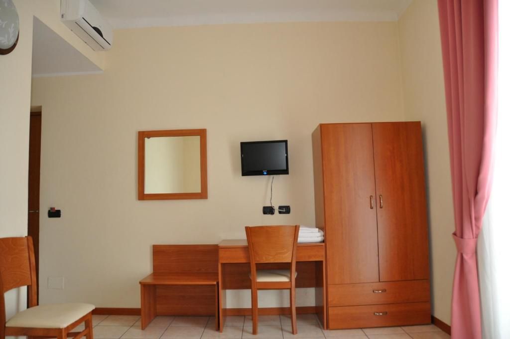 Um quarto com uma escrivaninha de madeira, uma cadeira, televisão fixada na parede e um guarda-roupa.