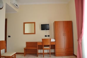 Um quarto com uma escrivaninha de madeira, uma cadeira, televisão fixada na parede e um guarda-roupa.