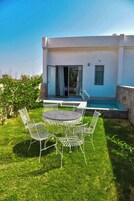 Um pátio moderno ao ar livre com uma mesa redonda e cadeiras, piscina e um edifício com porta de correr de vidro.