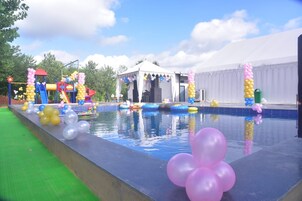 Área de piscina externa com escorrega e brinquedos infláveis, cercada por uma tenda branca e decorada com balões.