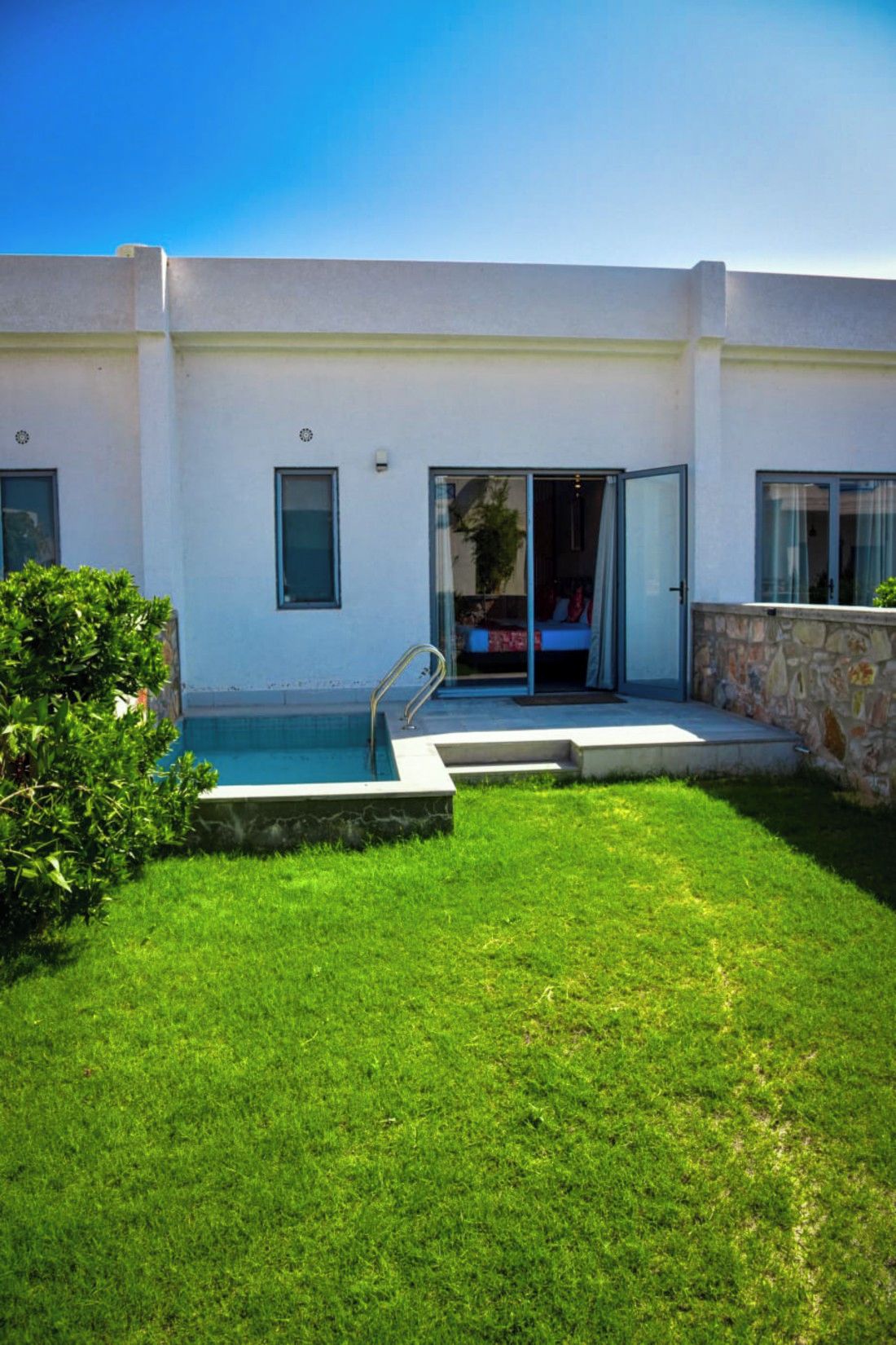Uma casa moderna com piscina, muro de pedra e gramado bem cuidado.
