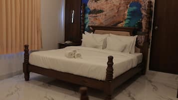 Cama bem arrumada com estrutura de madeira e roupa de cama branca, mesa de cabeceira com abajur e uma grande pintura de paisagem costeira na parede.
