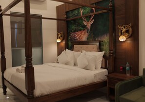 Uma cama com dossel, roupa de cama branca, cabeceira com pintura de tema florestal e duas luminárias de parede.