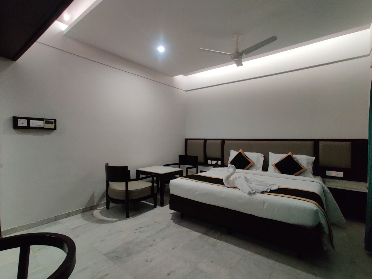 Quarto de hotel com cama, escrivaninha, cadeira e ventoinha no teto.