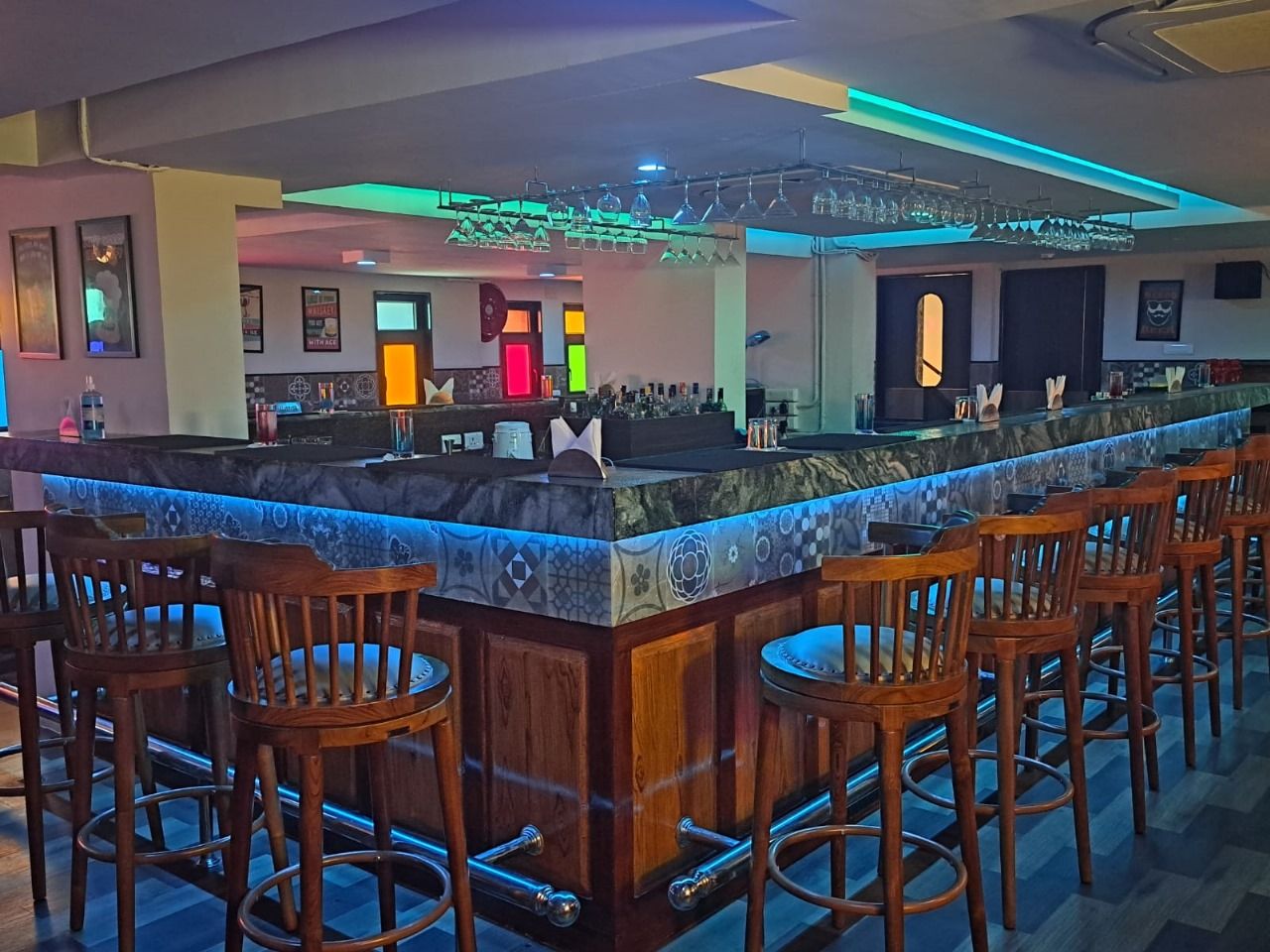Uma área de bar com um balcão comprido, vários bancos e uma variedade de garrafas e copos nas prateleiras.