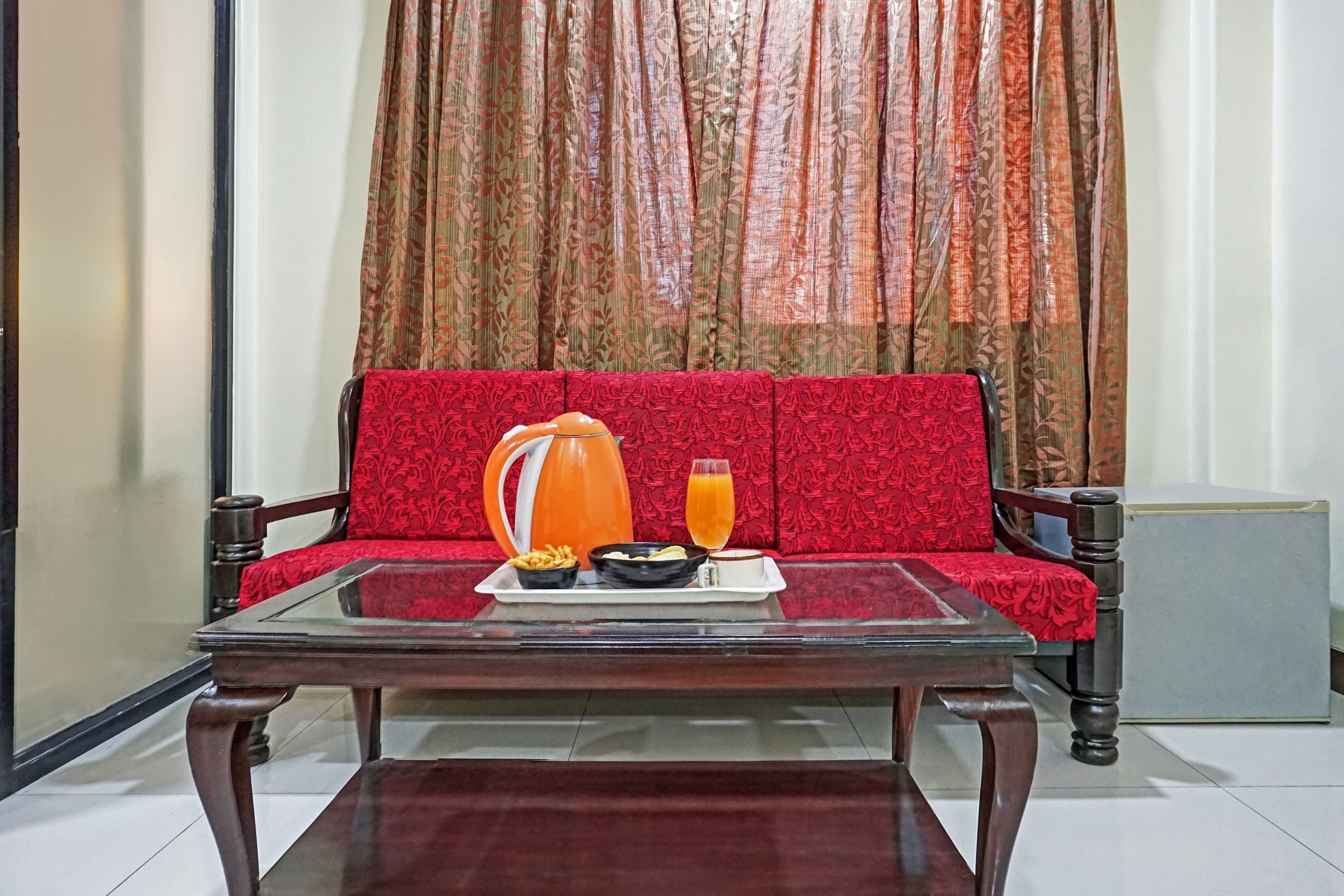 Quarto com sofá vermelho, mesa de centro de vidro e pequeno frigorífico.