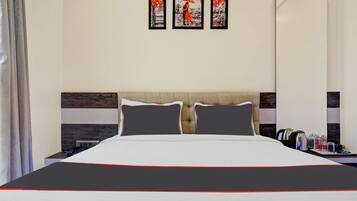 Quarto de hotel com cama, duas almofadas, mesa de cabeceira com telefone, cafeteira e bandeja com garrafas de água.