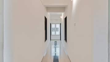 Um corredor comprido e estreito com piso refletivo, que leva a uma porta no final.