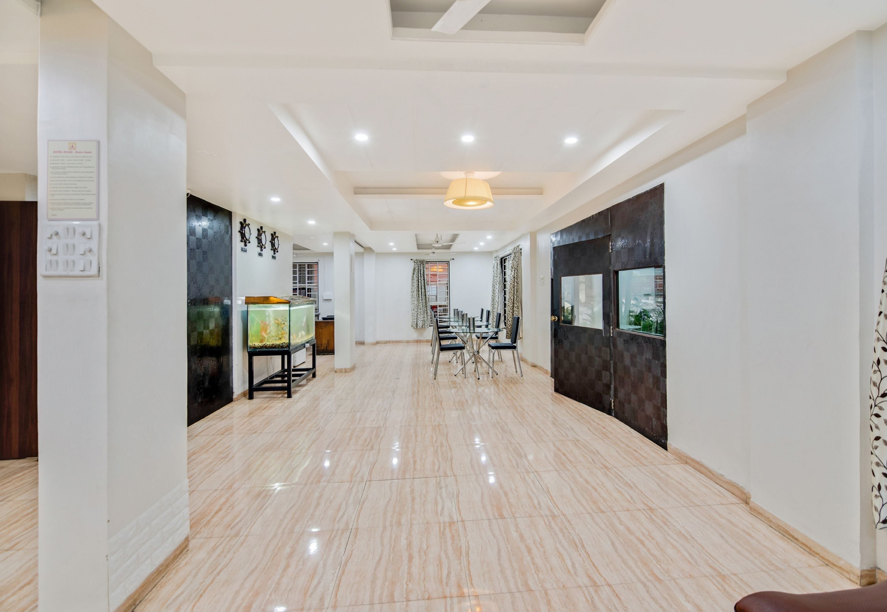 Um corredor amplo com piso de azulejos, uma sala de jantar com mesas e cadeiras, e teto com iluminação embutida.