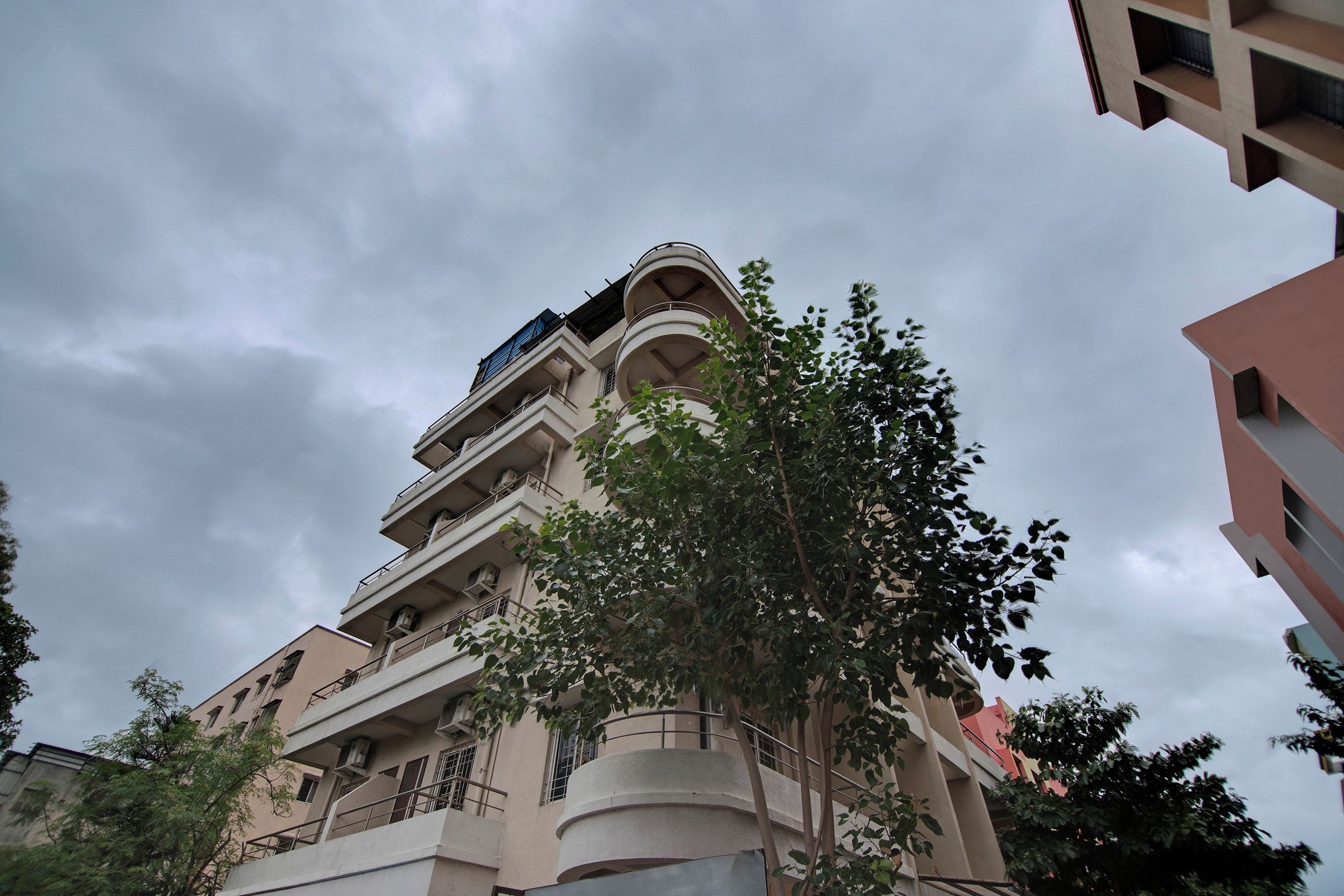 Edifício de vários andares com varandas e uma árvore em primeiro plano.