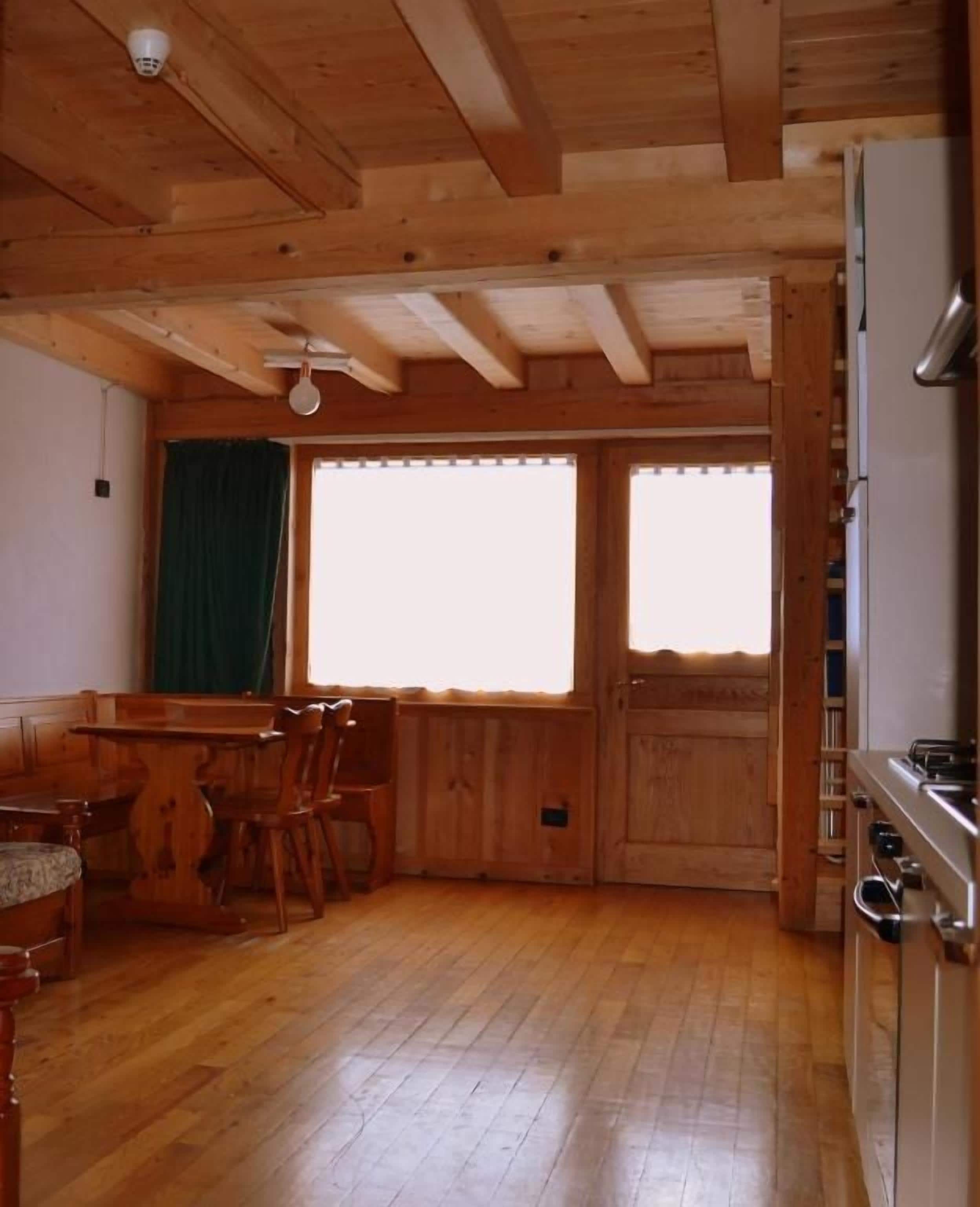 Interior em madeira com mesa de jantar, cadeiras, geladeira e janela.