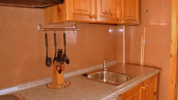Cozinha com armários de madeira, bancada de granito, pia de aço inoxidável e suporte para utensílios com diversas ferramentas de cozinha.