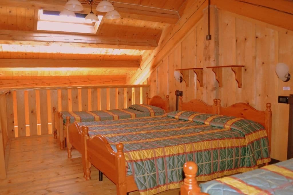 Quarto de cabana de madeira com duas camas, teto inclinado e claraboia.