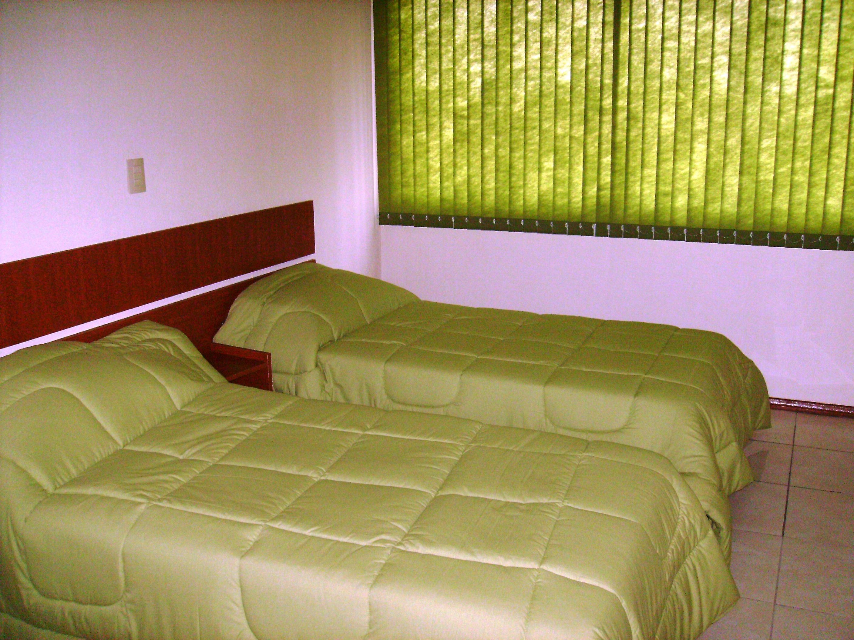 Quarto com duas camas, cabeceira de madeira, janela com persianas e piso de azulejos.