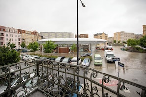 Rua urbana com carros estacionados, área de mercado coberta e edifícios ao fundo.