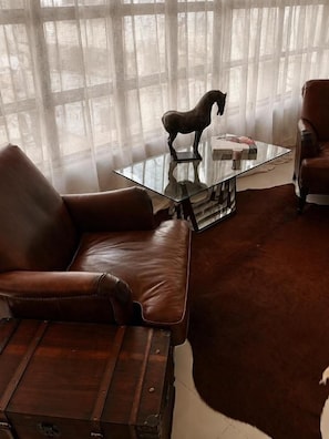 Quarto com sofá de couro, mesa de centro de vidro e tapete marrom.