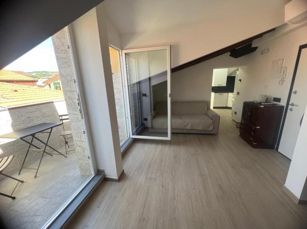 Quarto com porta de vidro deslizante para uma varanda, uma cama, cômoda e área de cozinha compacta.