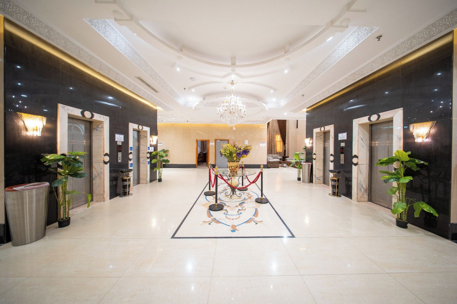 Um saguão de hotel com um lustre, plantas em vasos e uma barreira de corda vermelha.