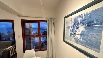 Quarto com uma janela grande, um quadro de barcos, um sofá e uma mesa de jantar.