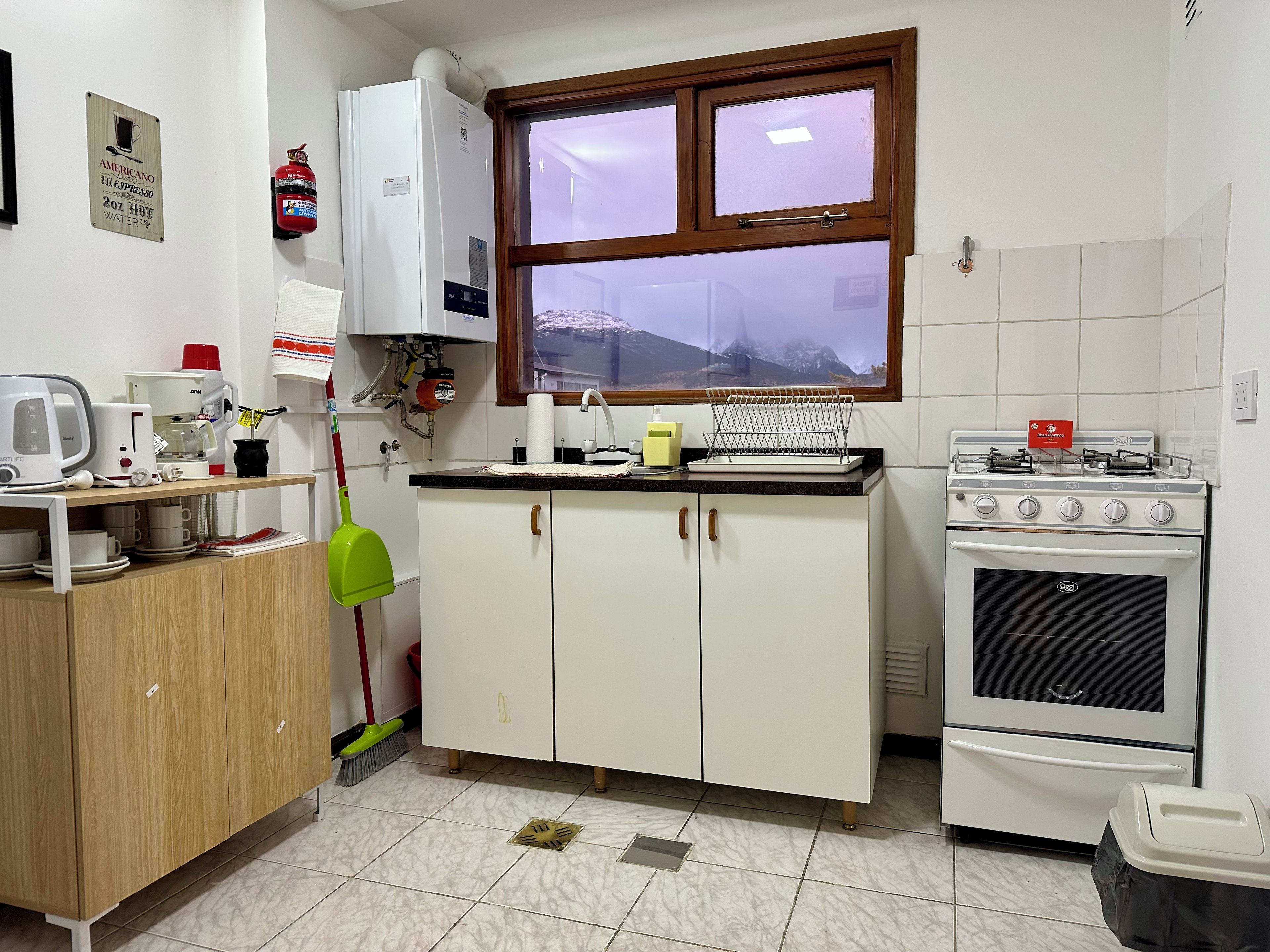 Cozinha com armários brancos, fogão, pia e janela com vista para montanhas.