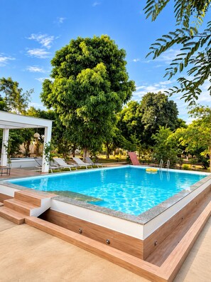 Piscina retangular com água azul cristalina, rodeada por um deck de madeira e uma pérgula branca.
