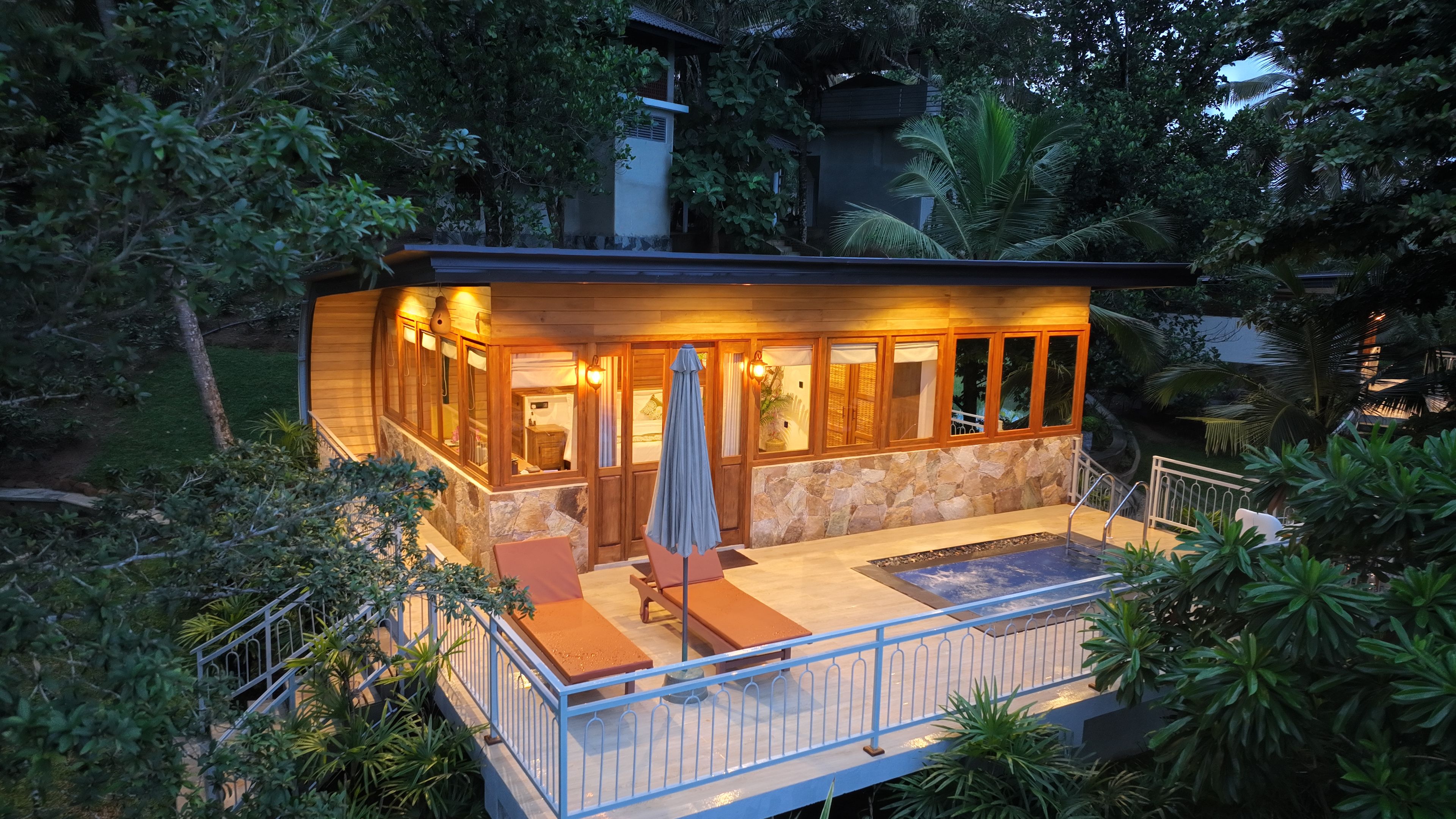 Uma cabana de madeira com fachada de pedra, uma varanda com assentos e uma área de piscina.