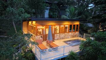 Uma cabana de madeira com fachada de pedra, uma varanda com assentos e uma área de piscina.