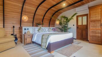 Quarto com teto de madeira curvo, cama com colcha estampada, uma guitarra, mesa de cabeceira e um vaso com planta.