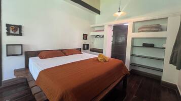 Quarto de hotel com cama, guarda-roupa, um banco e luminária pendente.