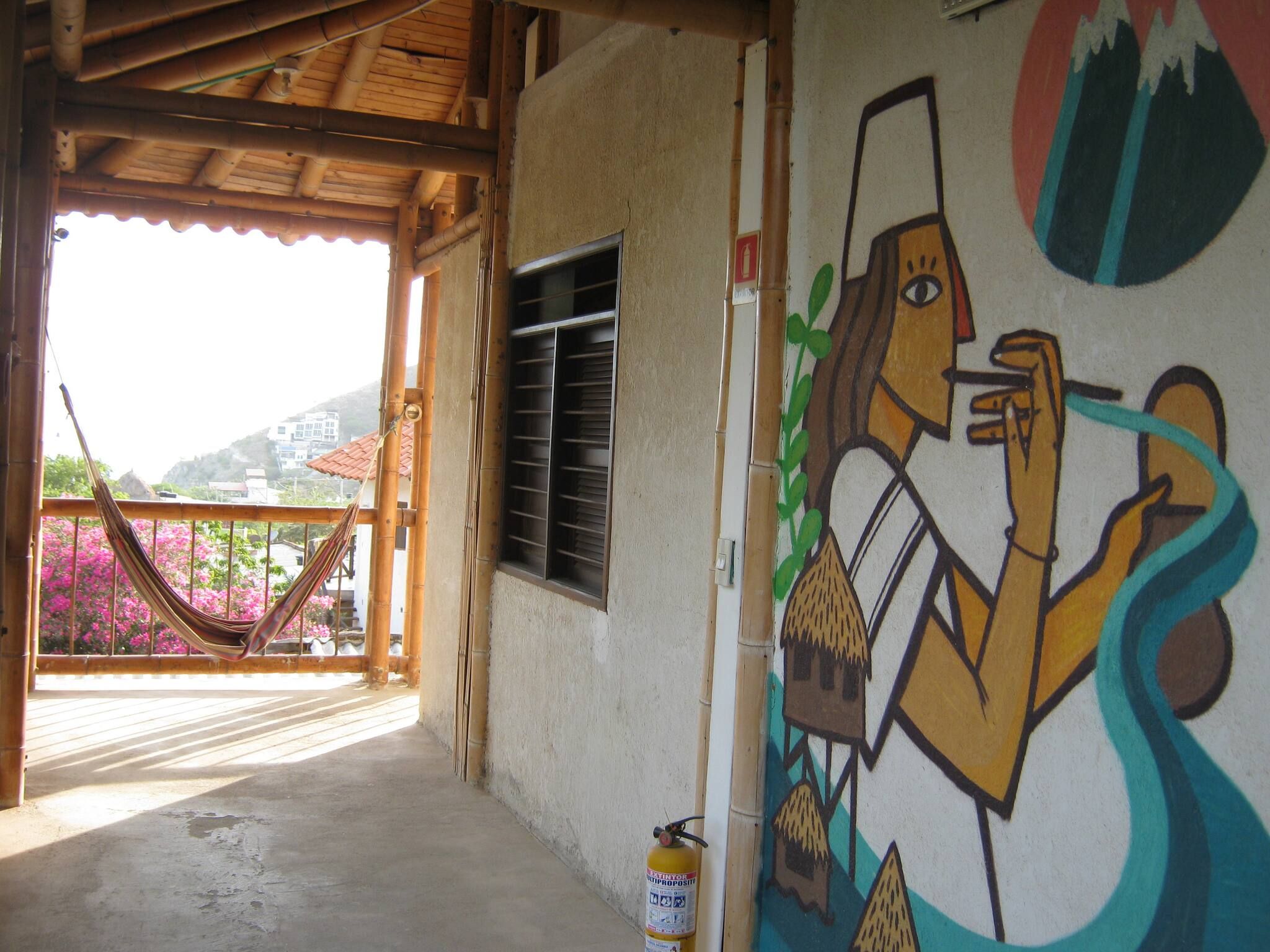 Um quarto com uma rede, uma janela com persianas e um mural na parede.