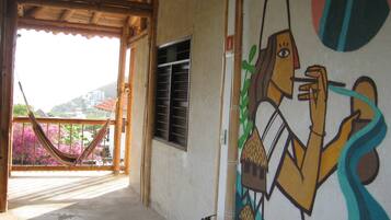Um quarto com uma rede, uma janela com persianas e um mural na parede.