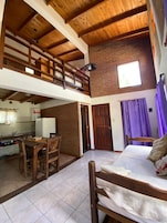 Quarto amplo com teto alto, varanda, área de refeições com móveis de madeira e vista para uma cozinha.