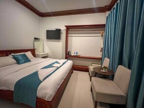 Quarto de hotel com uma cama grande, mesa de cabeceira, cadeira, pequena mesa com uma planta e janela com cortinas.